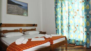 Uma cama de casal com lençóis brancos e um cobertor laranja xadrez, uma cabeceira de madeira e um quadro com uma paisagem de praia na parede.