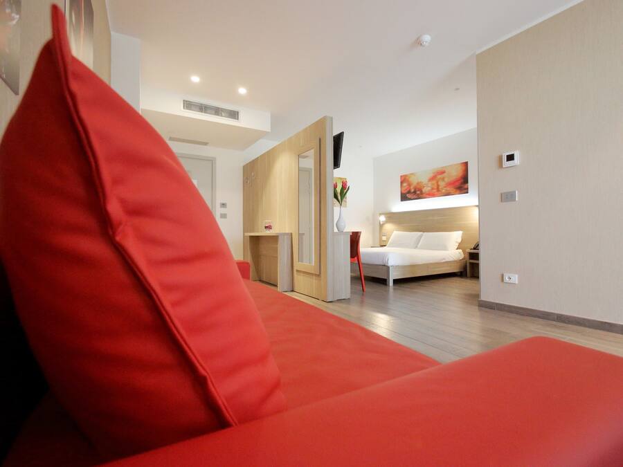 Quarto de hotel moderno com um sofá vermelho, uma cama branca e um chão de madeira.
