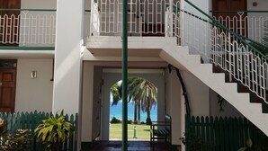 Um edifício com vários níveis, uma escadaria central, varandas com guarda-corpos brancos e vista para o oceano através de um arco aberto.