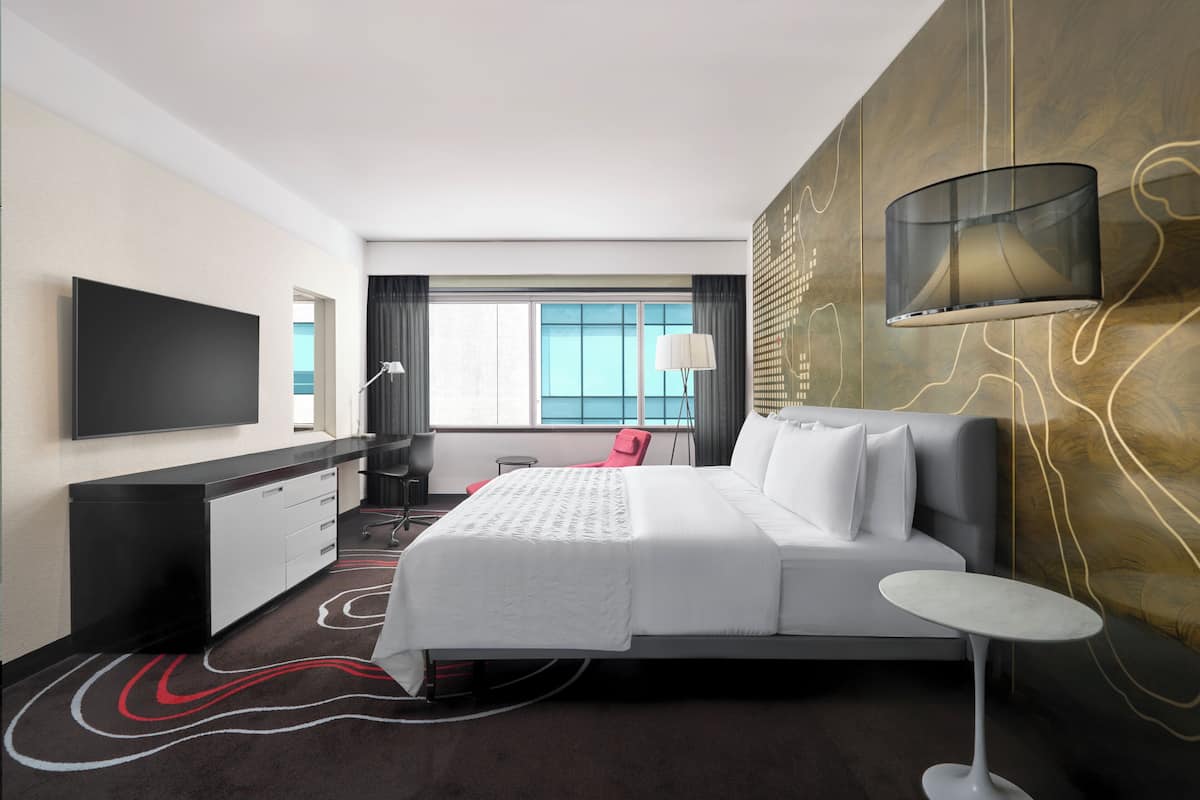 Quarto de hotel moderno com uma cama grande, uma TV de tela plana, uma escrivaninha e uma cadeira.