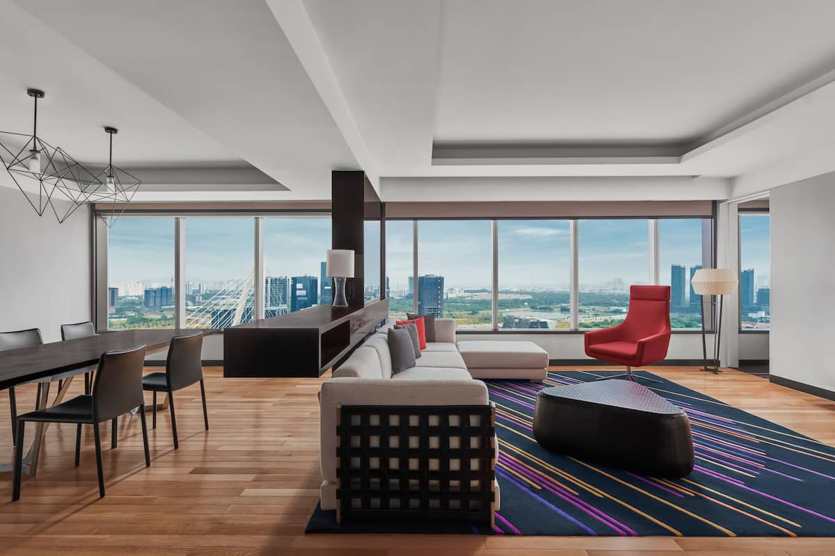 Uma sala de estar moderna com uma grande janela, um sofá, uma poltrona vermelha e uma área de jantar com cadeiras e uma mesa.
