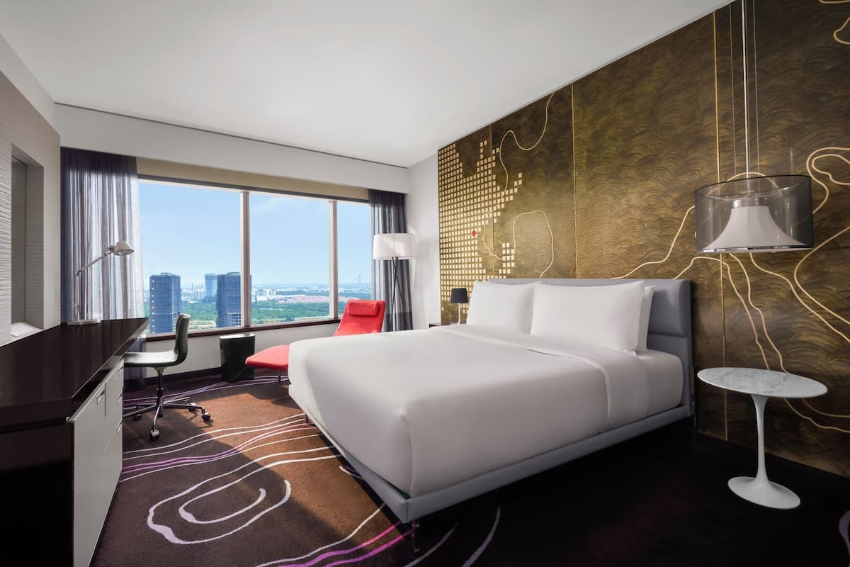 Quarto de hotel com uma cama grande, uma escrivaninha, uma cadeira, uma mesinha e vista para a cidade.