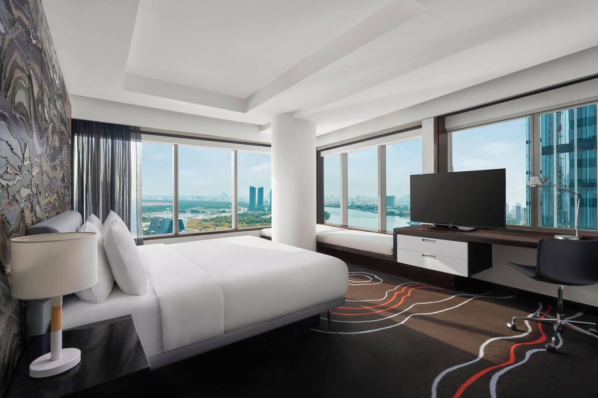 Quarto de hotel moderno com uma cama grande, televisão de tela plana, escrivaninha e vista para a cidade.