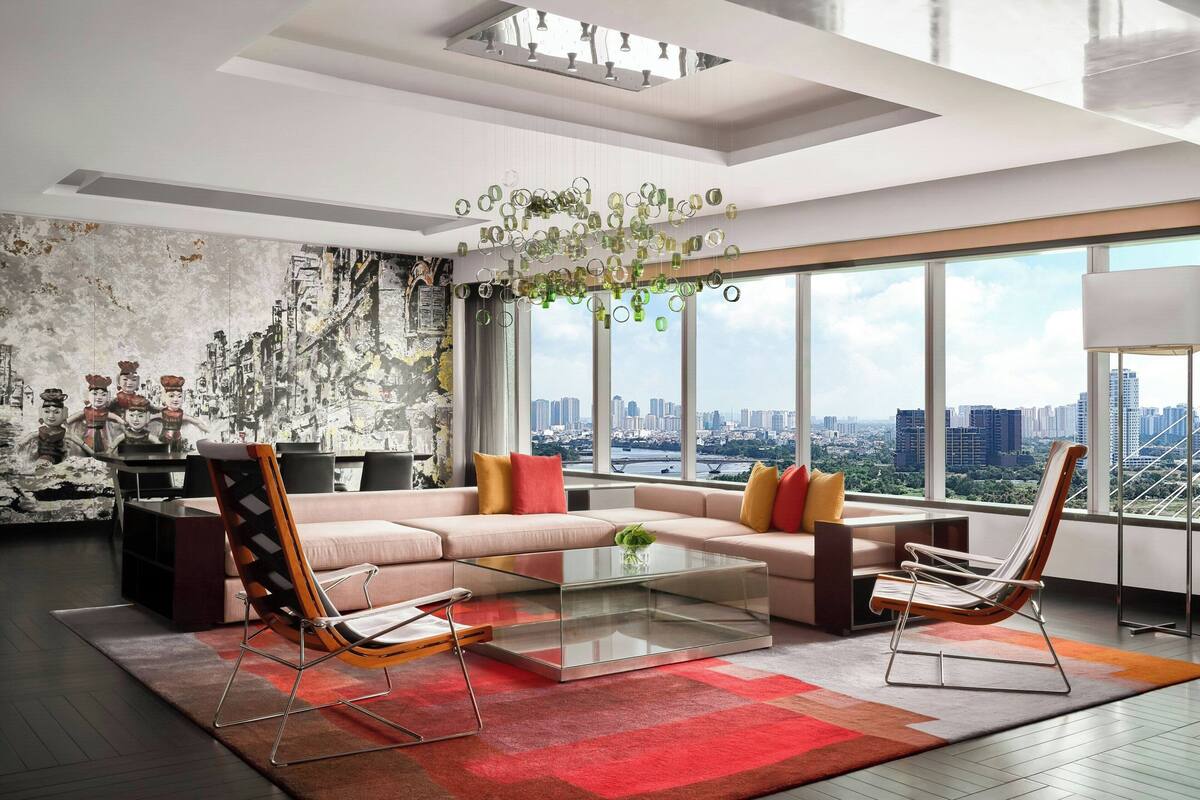 Uma sala de estar moderna com uma mesa de centro de vidro, duas poltronas de couro, um sofá e vista para a cidade através de grandes janelas.