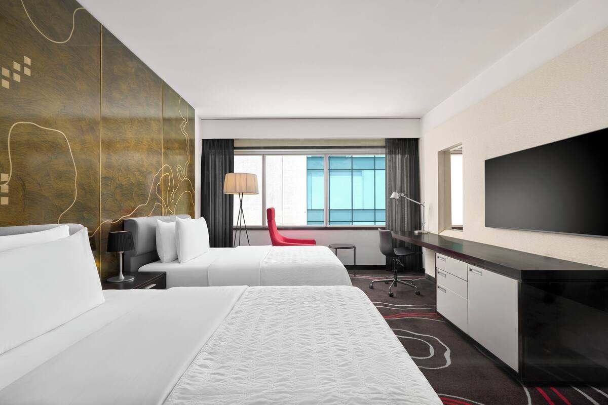 Quarto de hotel com duas camas, uma mesa, uma televisão e vista para a cidade.