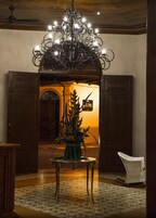 Um candelabro com várias luzes, uma planta decorativa sobre uma mesa e um chão com padrão.