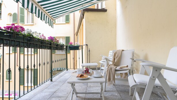 Varanda com mesa posta para dois, cadeiras brancas e toldo riscado.