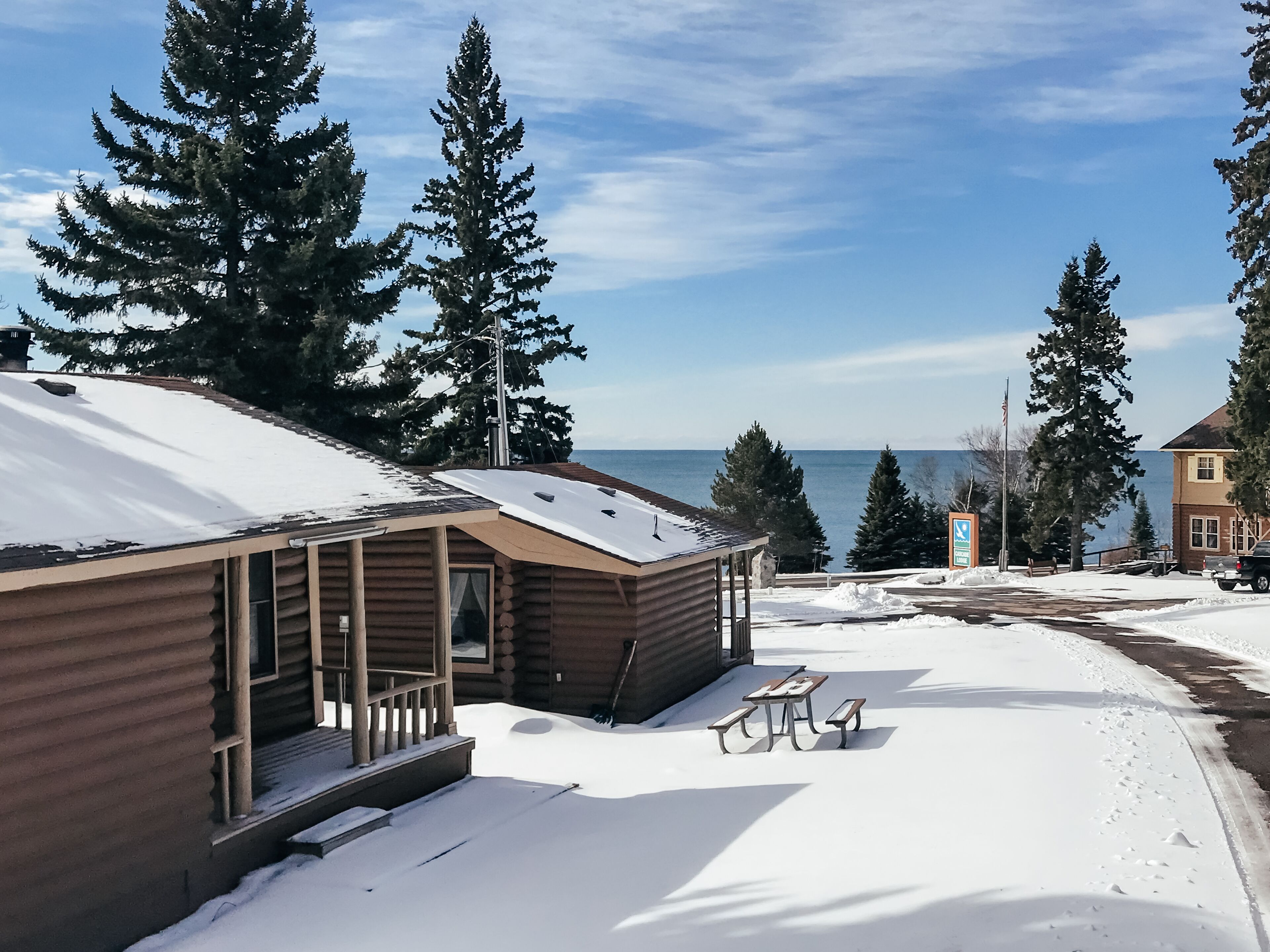 Uma cabana com telhado coberto de neve, um deck de madeira e vista para o oceano.