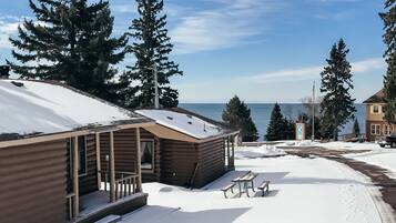 Uma cabana com telhado coberto de neve, um deck de madeira e vista para o oceano.