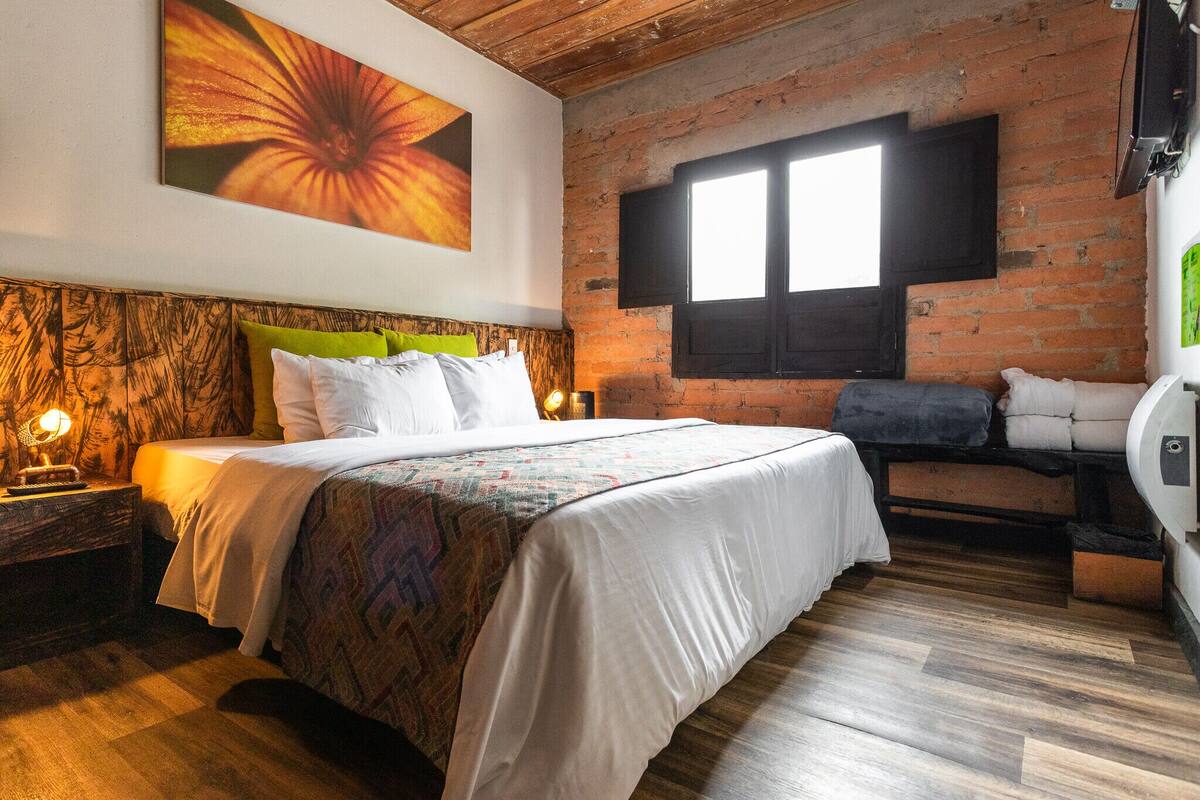 Quarto com uma cama grande, cabeceira de madeira, parede de tijolos e uma janela com persianas.