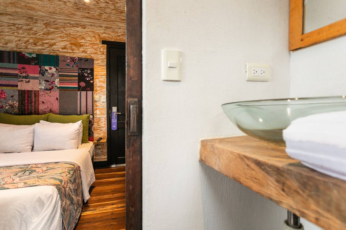 Quarto com cabeceira de madeira, cama com colcha florida e arte abstrata colorida na parede.