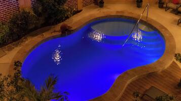 Piscina iluminada com luz azul, cercada por um espaço de estar com cadeiras e plantas.