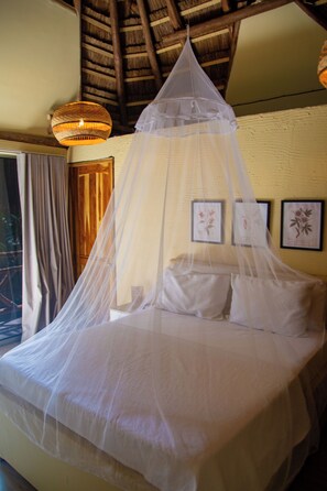 Uma cama com dossel, luminária pendente e gravuras botânicas emolduradas na parede.