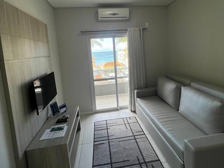 Uma sala de estar moderna com televisão de tela plana, um sofá, uma mesinha e vista para o oceano por uma porta de vidro deslizante.