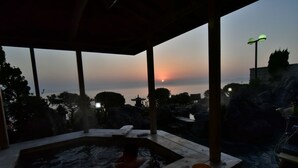 Uma área de hidromassagem com vista para o pôr do sol, deck de madeira e detalhes em pedra.