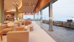 Um lobby de hotel moderno com uma extensa área de estar, grandes janelas e vista para o mar.