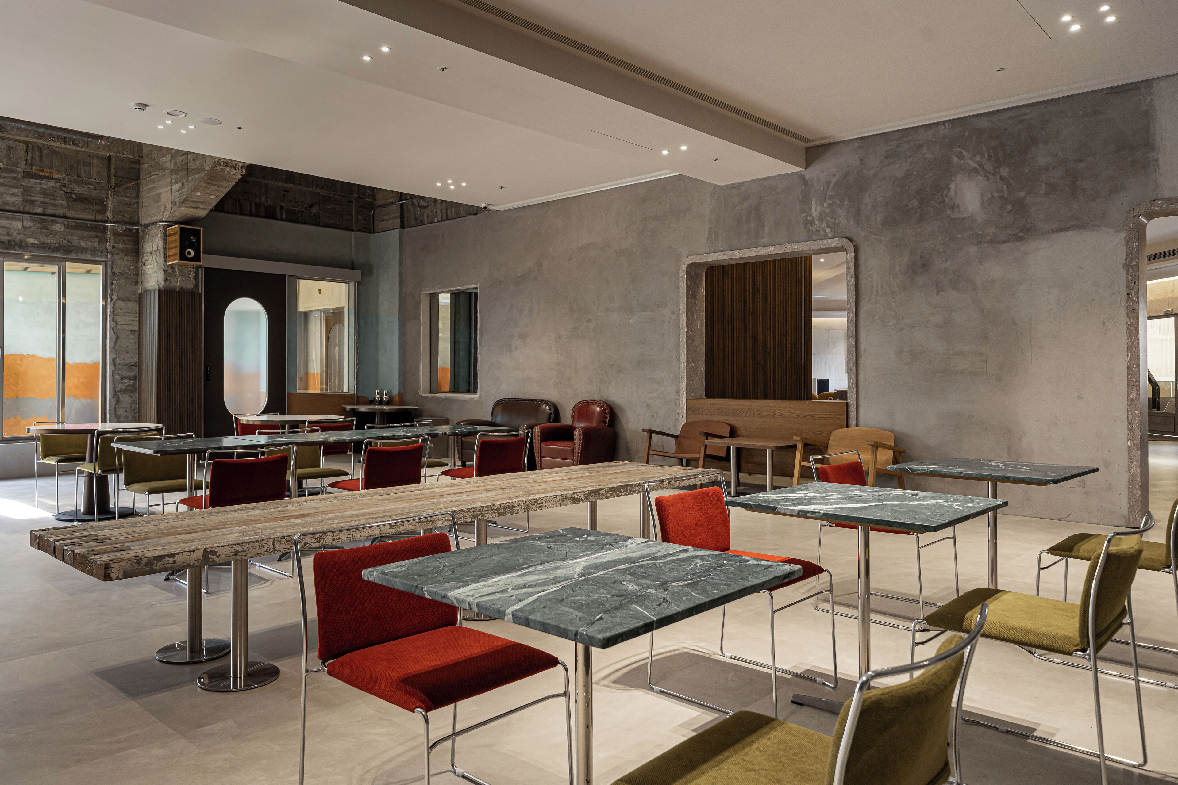 Uma sala de jantar moderna com várias mesas e cadeiras, uma mesa de madeira comprida e um espelho grande na parede.