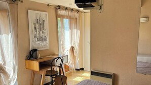 Quarto com cama, escrivaninha, cadeira, televisão e janela com cortinas.
