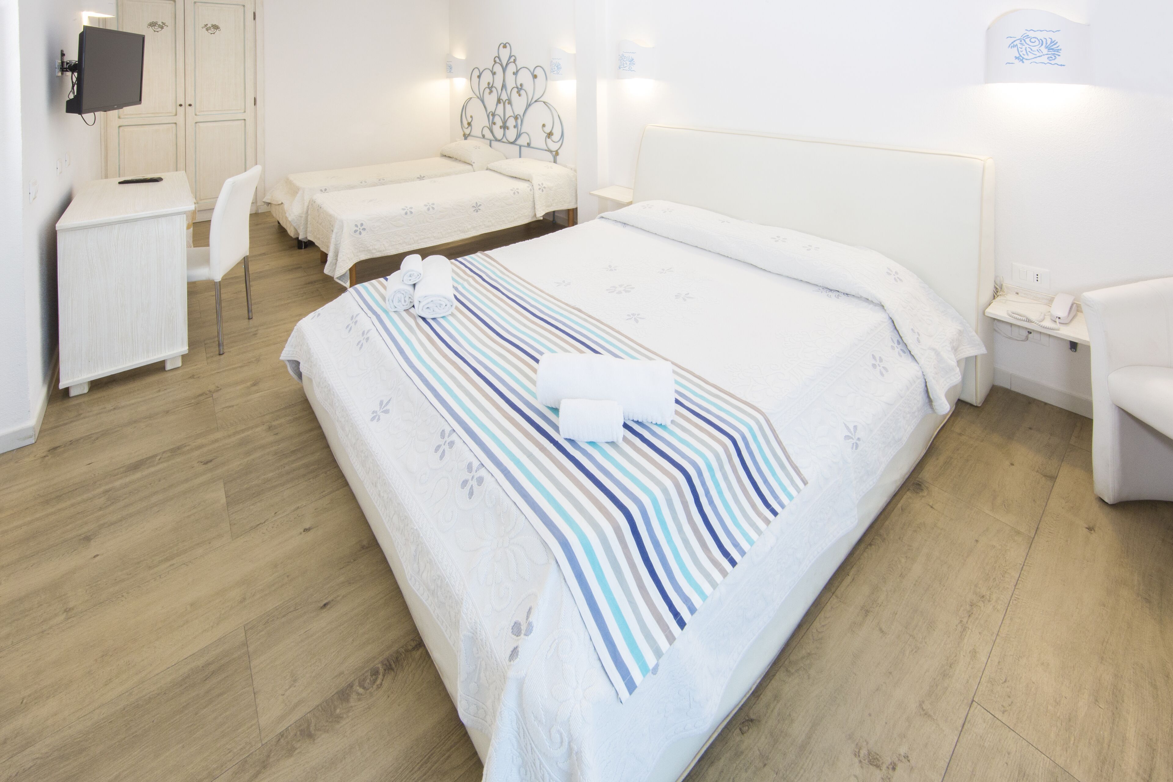 Quarto de hotel com uma cama grande, duas mesas de cabeceira, uma escrivaninha com cadeira, televisão e um guarda-roupa.