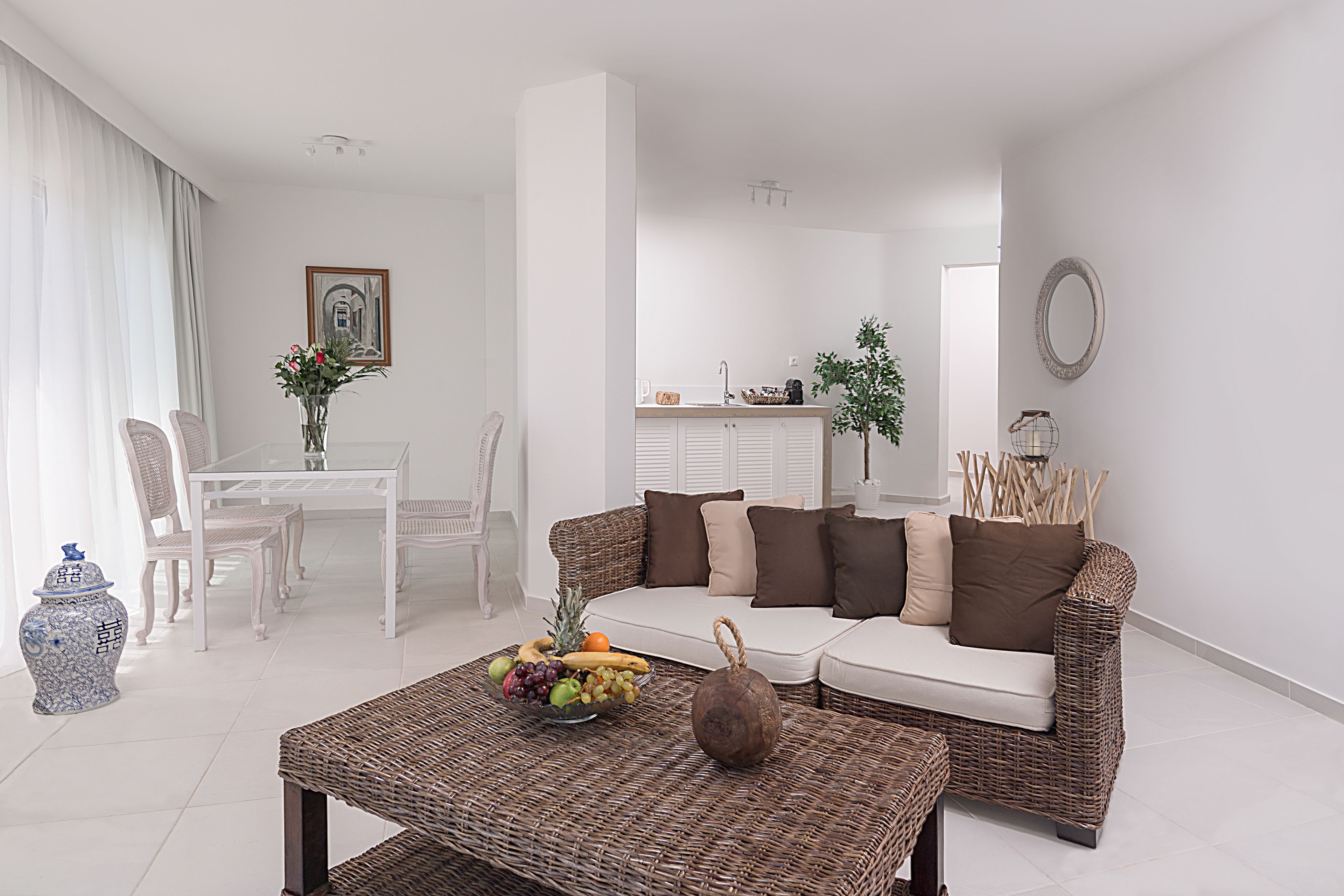 Uma sala moderna com uma mesa de centro de vime, sofá branco e área de refeições com cadeiras e uma mesa.