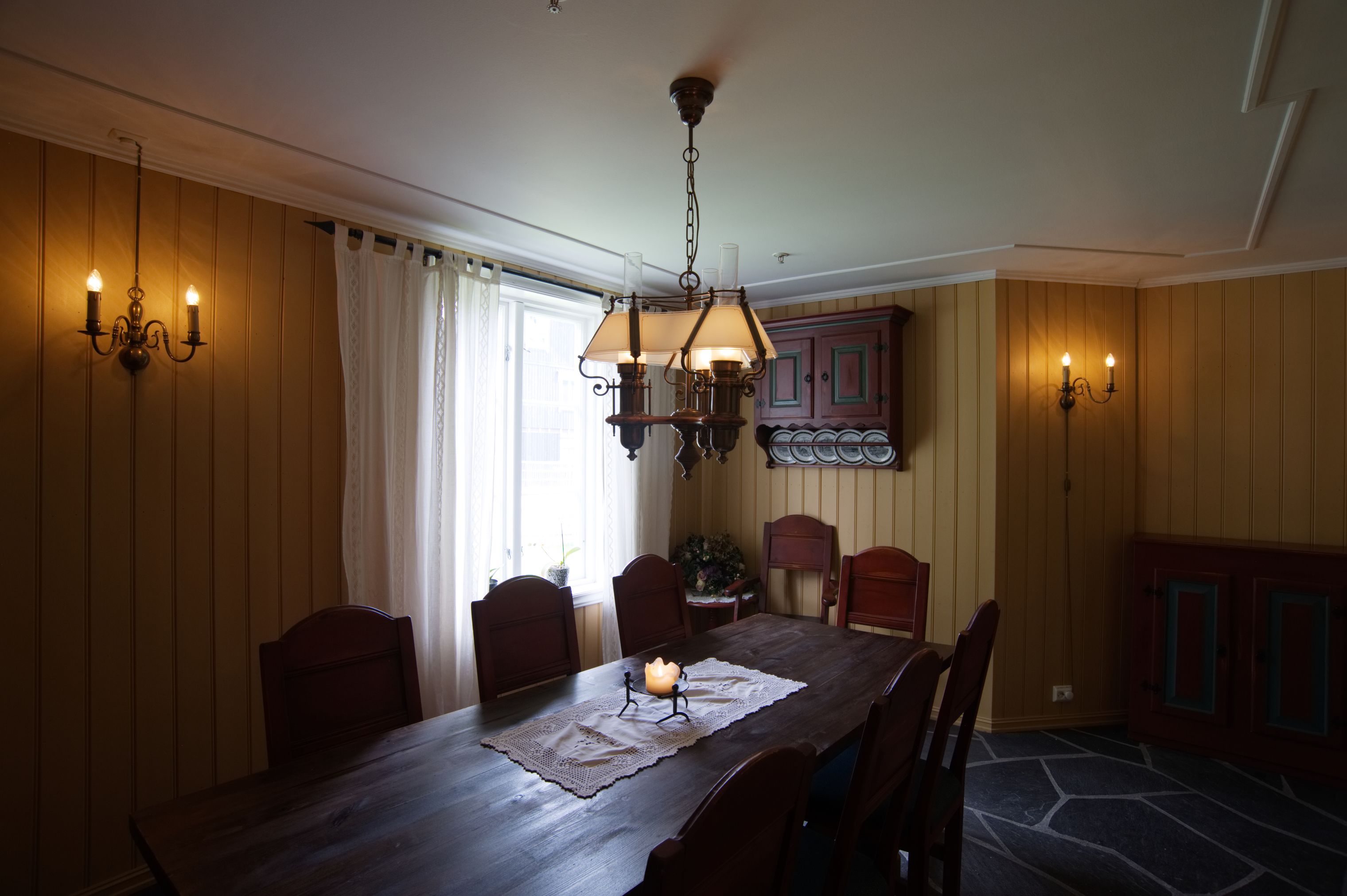 Uma sala de jantar com uma mesa de madeira, cadeiras, um candelabro e arandelas.