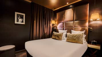 Quarto de hotel com uma cama grande, cabeceira com painéis, mesa de cabeceira com abajur e um quadro pendurado na parede.