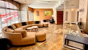 Uma área de recepção moderna com um sofá curvo, pequenas mesas redondas e um balcão de atendimento.