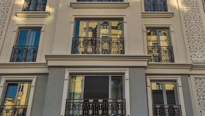 Um hotel com vários andares e fachada simétrica, com múltiplas varandas e grades ornamentadas, e uma entrada destacada com um anúncio.