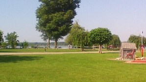 Um parque com grama verde, árvores, um pequeno galpão e um mastro.