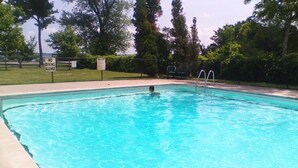 Piscina transparente com placa indicando que mergulhos não são permitidos, cercada por árvores e um gramado.