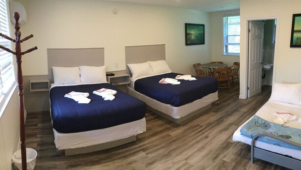 Quarto de hotel com duas camas, uma mesa de jantar pequena e uma porta que dá para outro cômodo.