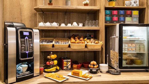 Buffet de café da manhã com máquina de café, pães, doces, frutas e bebidas.
