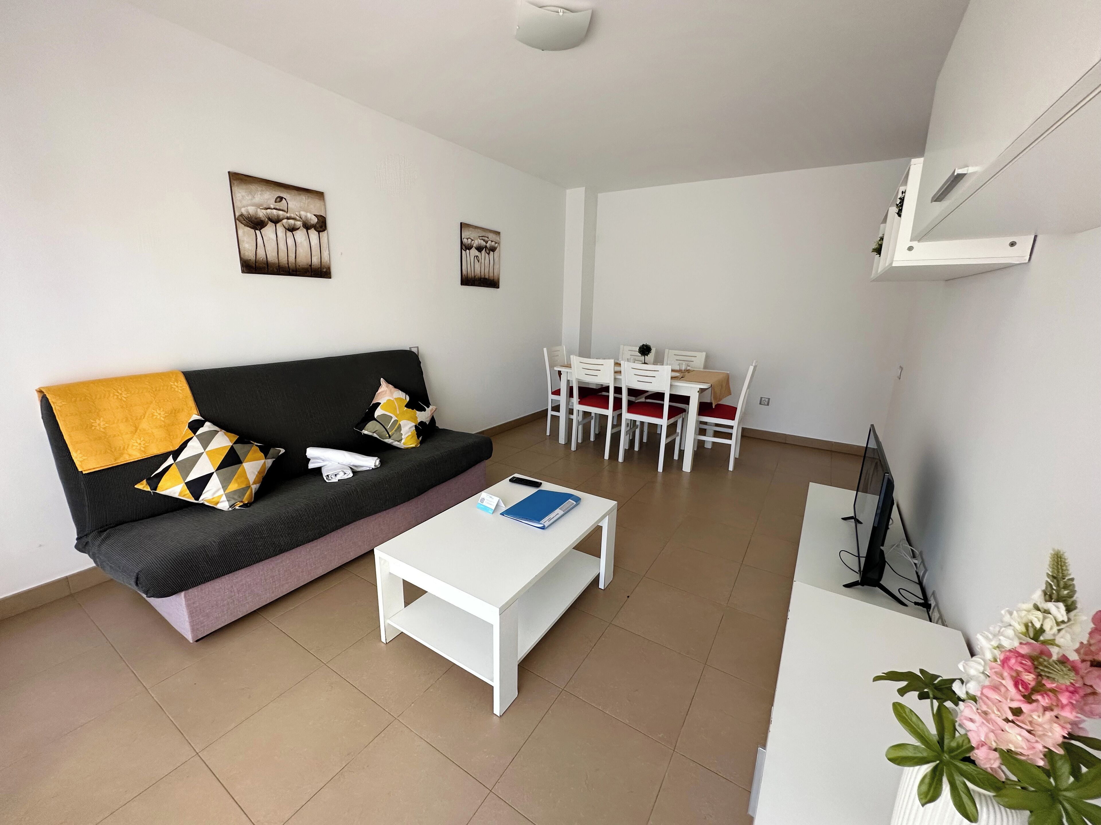 Uma sala de estar moderna com um sofá preto, mesa de centro branca e um espaço de jantar com cadeiras e mesa brancas.