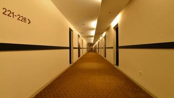 Corredor de hotel com piso coberto por carpete e portas em ambos os lados, identificadas com os números dos quartos de 221 a 226.