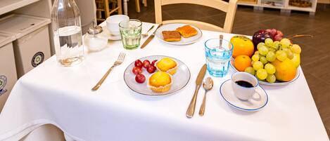 Uma área de refeições com uma mesa posta para o café da manhã, incluindo frutas, pão e bebidas.