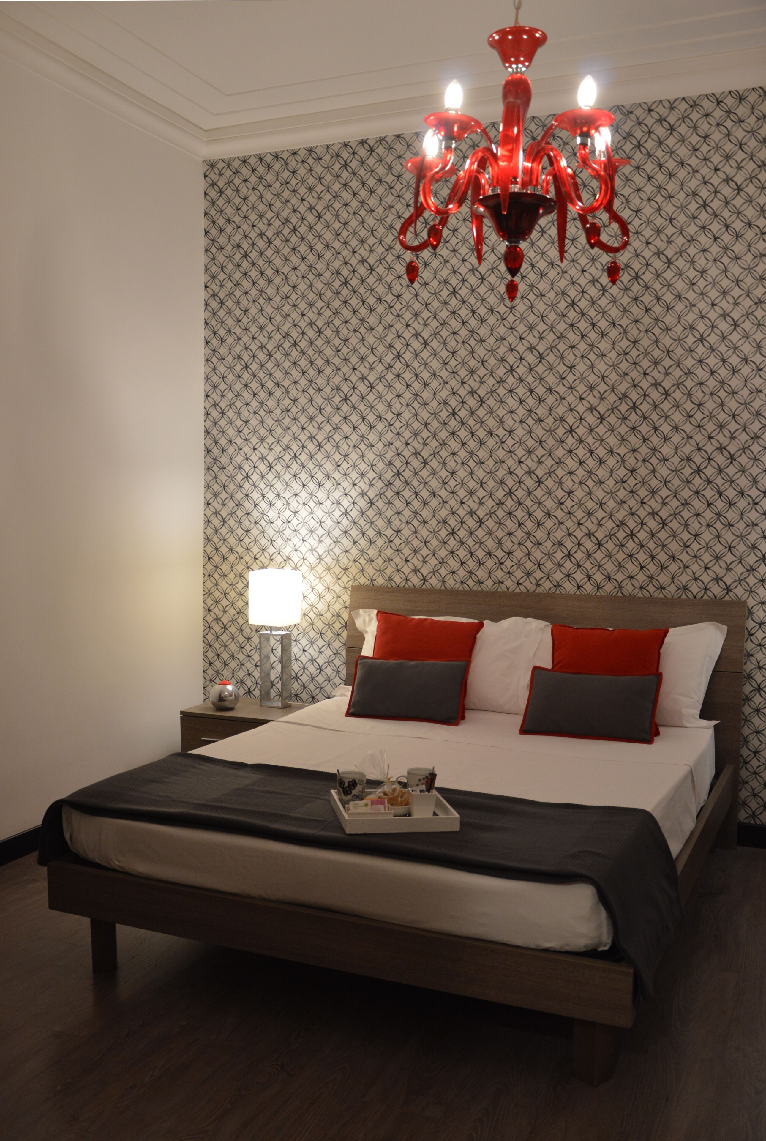 Cama bem arrumada com um suporte de objetos, luminária de cabeceira e papel de parede estampado.