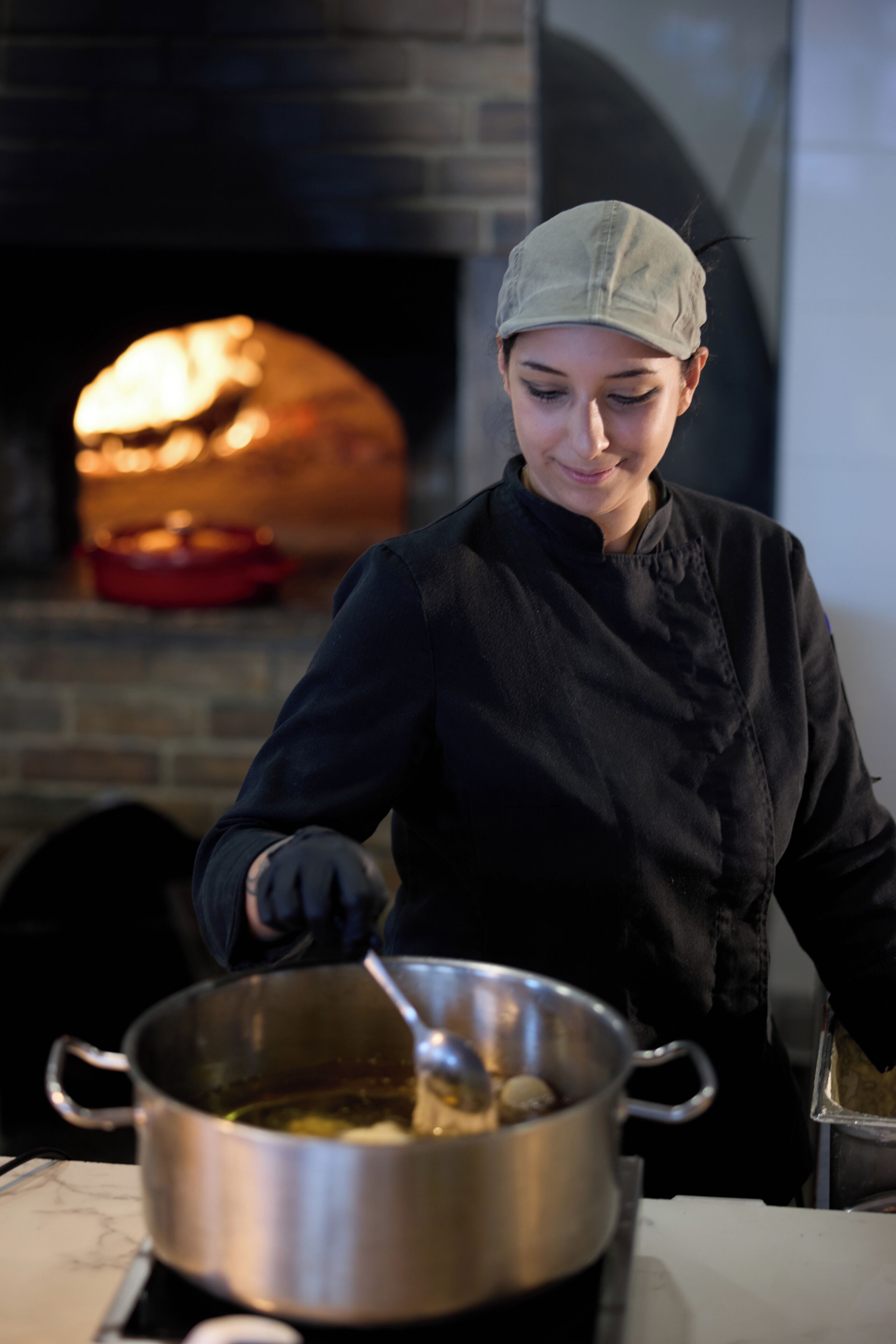 Uma pessoa cozinhando em uma cozinha com um forno de tijolos ao fundo.