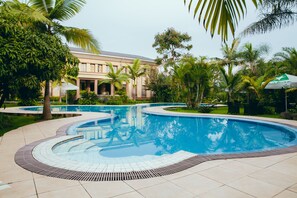 Piscina com design curvo, cercada por palmeiras e um edifício com colunas.