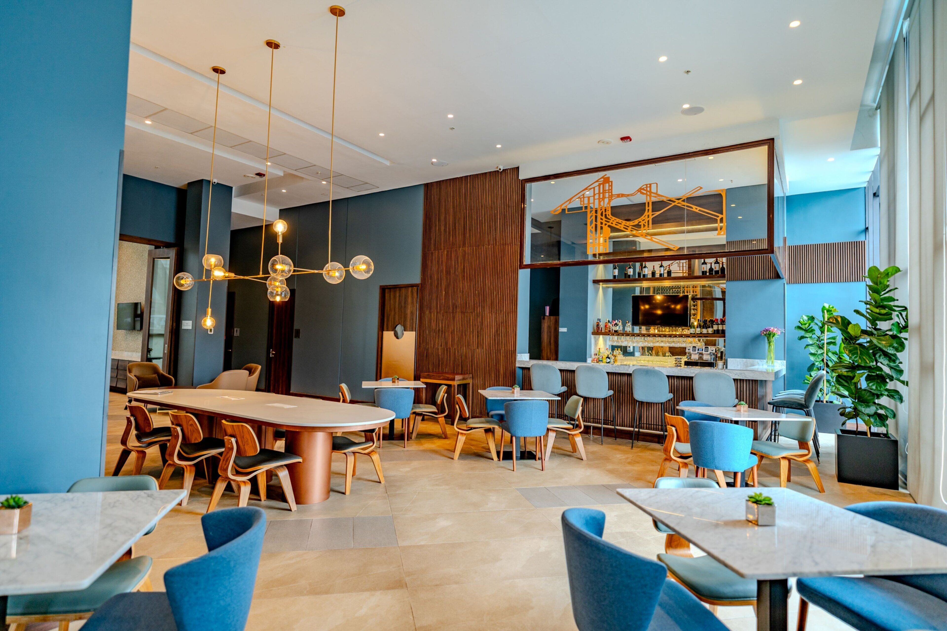 Um restaurante moderno com área de bar, mesas de madeira e cadeiras azuis.