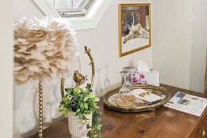 Uma mesa de madeira com uma bandeja decorativa, um vaso com folhagem verde, um objeto branco e fofo, um enfeite de pássaro dourado e um quadro na parede.