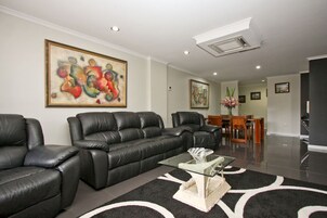 Uma sala de estar moderna com um sofá de couro preto, uma mesa de centro de vidro e uma grande pintura abstrata na parede.
