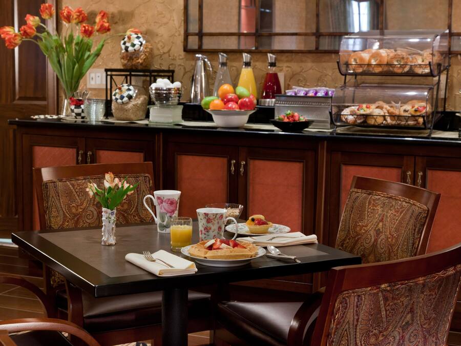 Uma mesa de café da manhã com uma tigela de frutas, suco e pães.