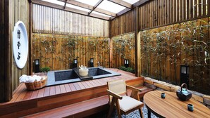 Uma área de spa em madeira com hidromassagem, assentos e plantas de bambu.