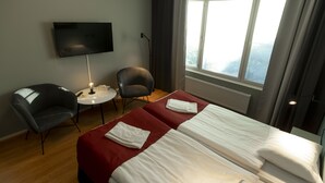 Quarto de hotel com duas camas, televisão, secretária, duas cadeiras e janela com cortinas.
