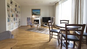 Uma sala de estar com lareira, televisão, estante de livros e área de jantar com cadeiras e mesa.