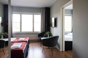 Quarto de hotel com uma cama, uma escrivaninha com cadeira, televisão e janela com cortinas.