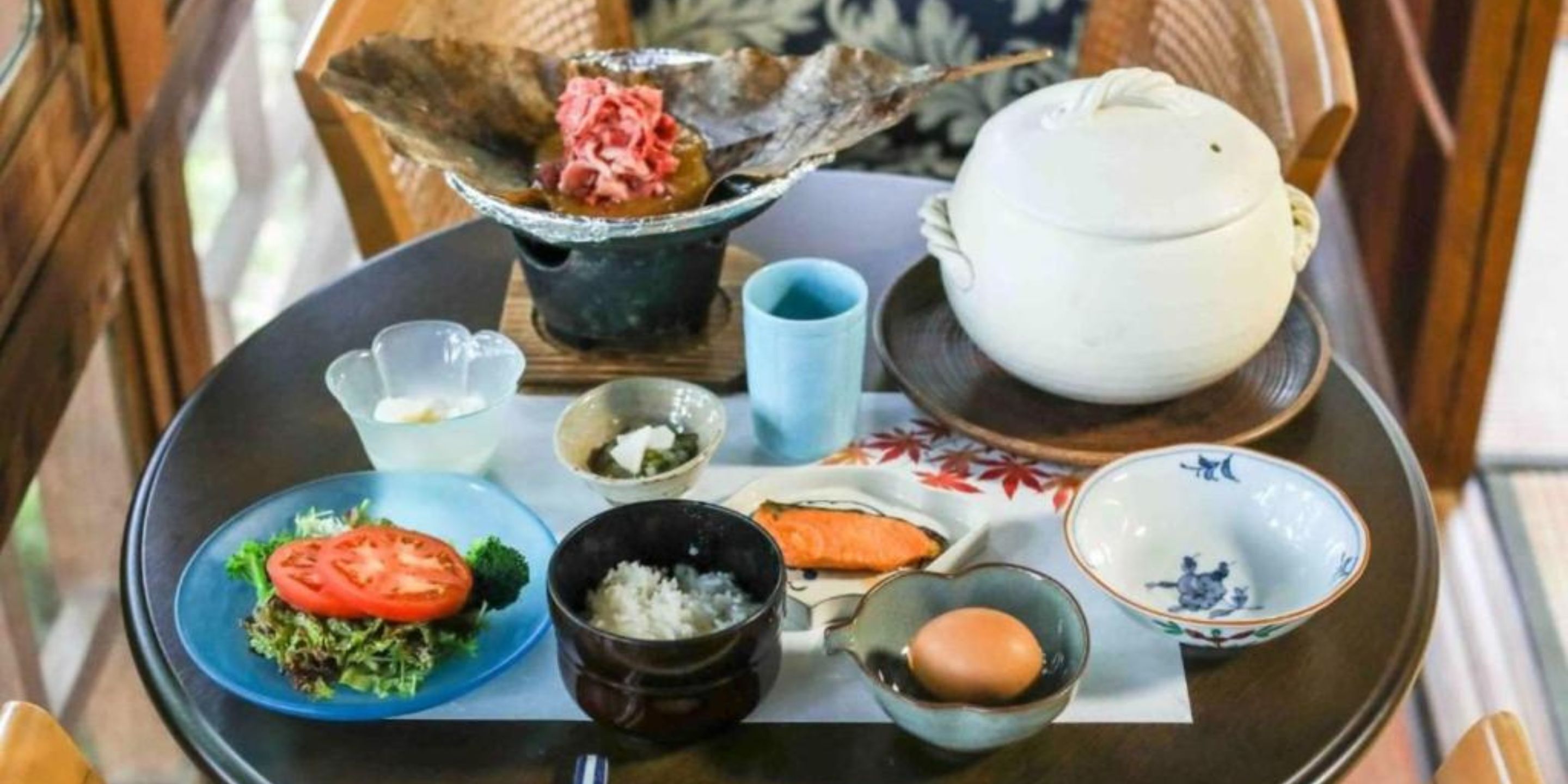 Uma mesa de jantar com diversos pratos, incluindo uma tigela de arroz, um prato de salada, uma sopa e um pote de ensopado.