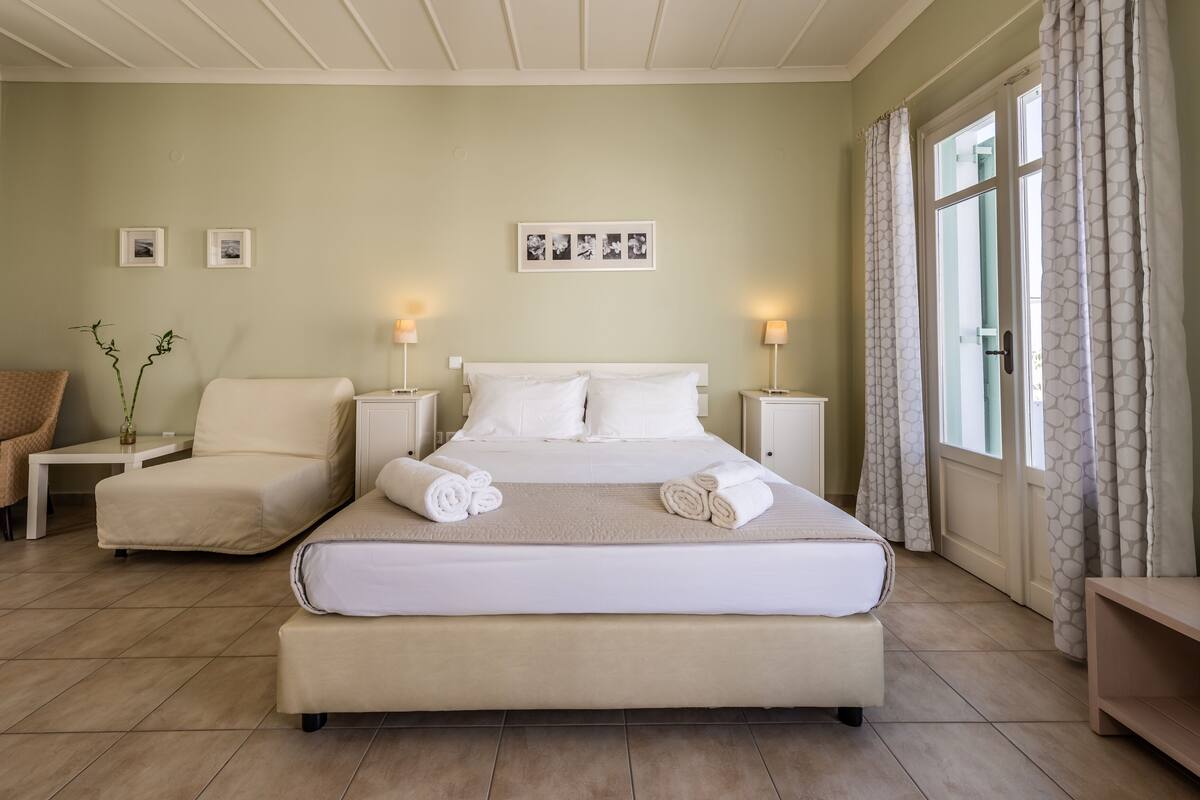 Quarto com uma cama grande, duas mesas de cabeceira, uma cadeira e uma mesinha.