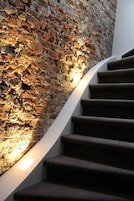 Uma escadaria com uma parede de tijolos texturizados de um lado e uma parede branca do outro.