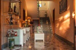 Um corredor com uma vitrine de vidro, mobiliário de vime, uma escadaria e um vaso com flores.